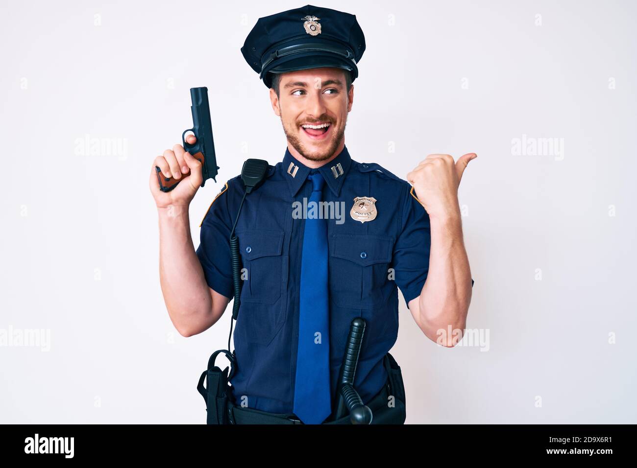 Young caucasian man wearing police uniform holding gun pointing thumb ...