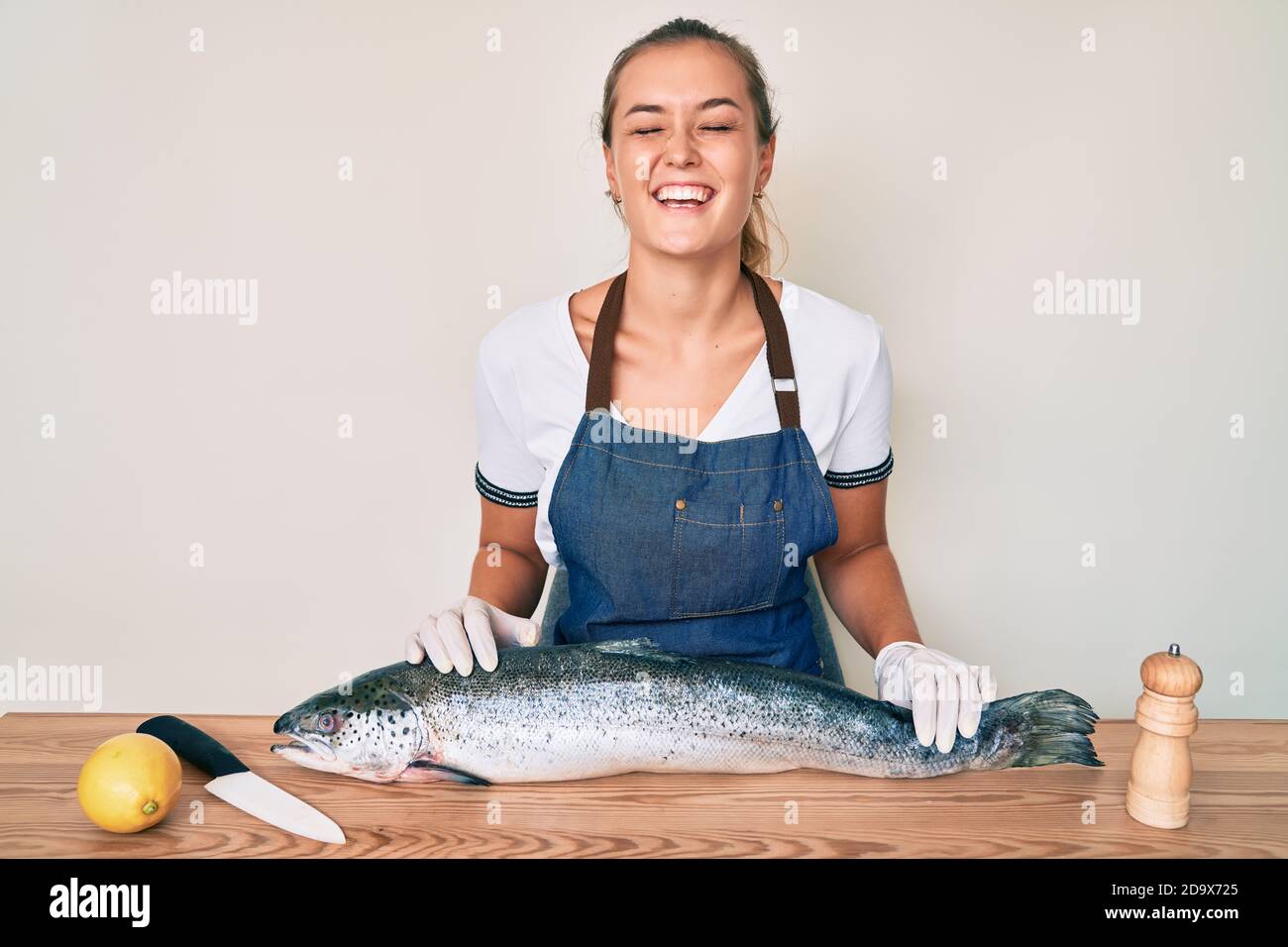 Beautiful caucasian woman fishmonger selling fresh raw salmon smiling and laughing hard out loud ...