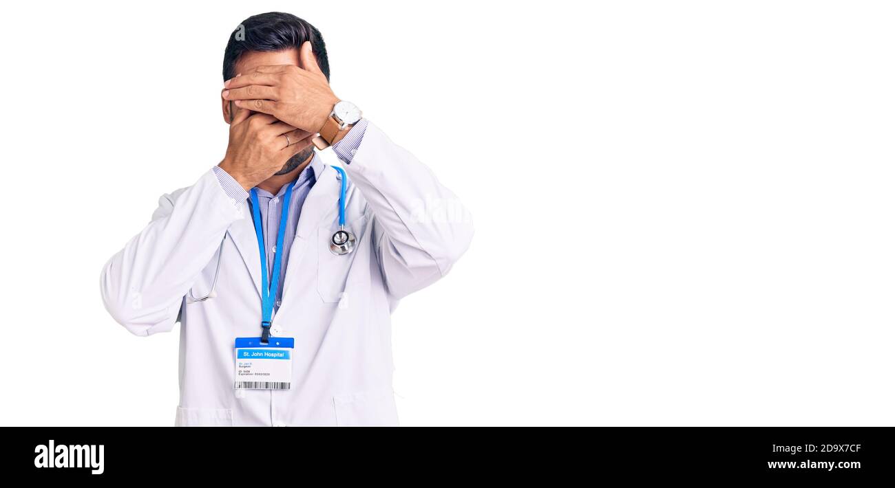Young hispanic man wearing doctor uniform and stethoscope covering eyes ...
