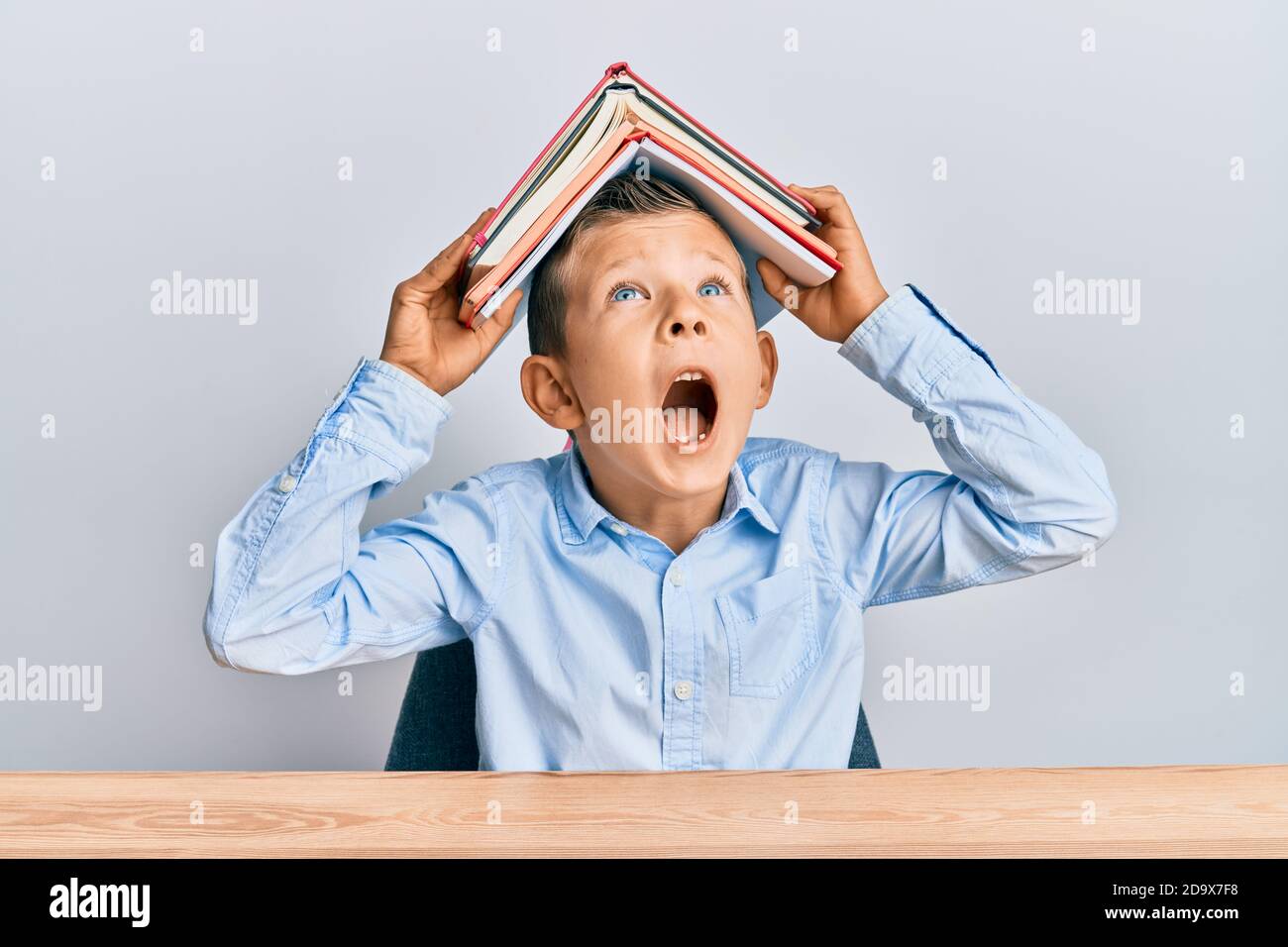 Adorable caucasian kid holding book on head angry and mad screaming ...