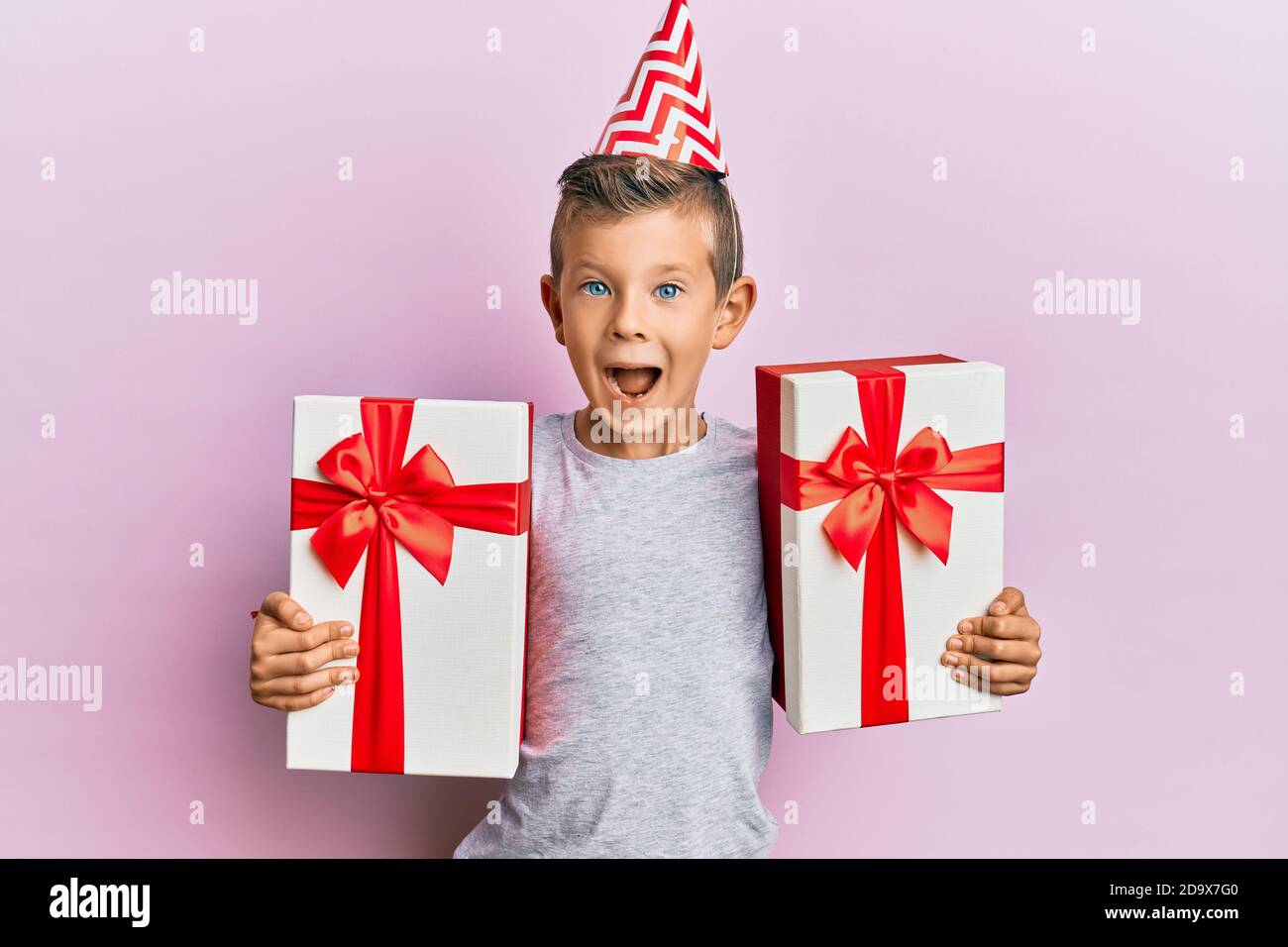 Adorable caucasian kid wearing birthday hat holding presents ...
