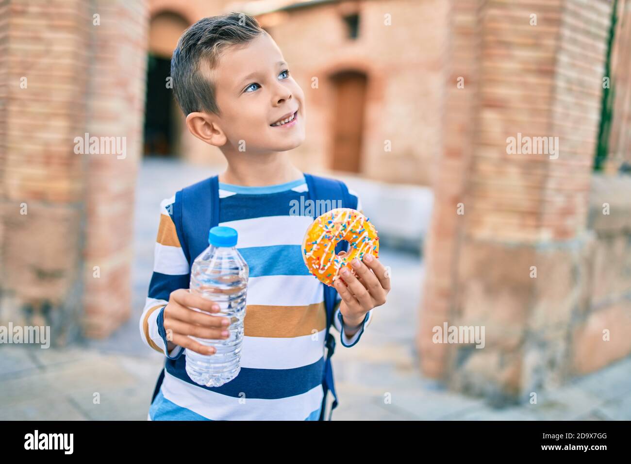 Adorable caucasian student boy smiling happy holding donut and bottle ...