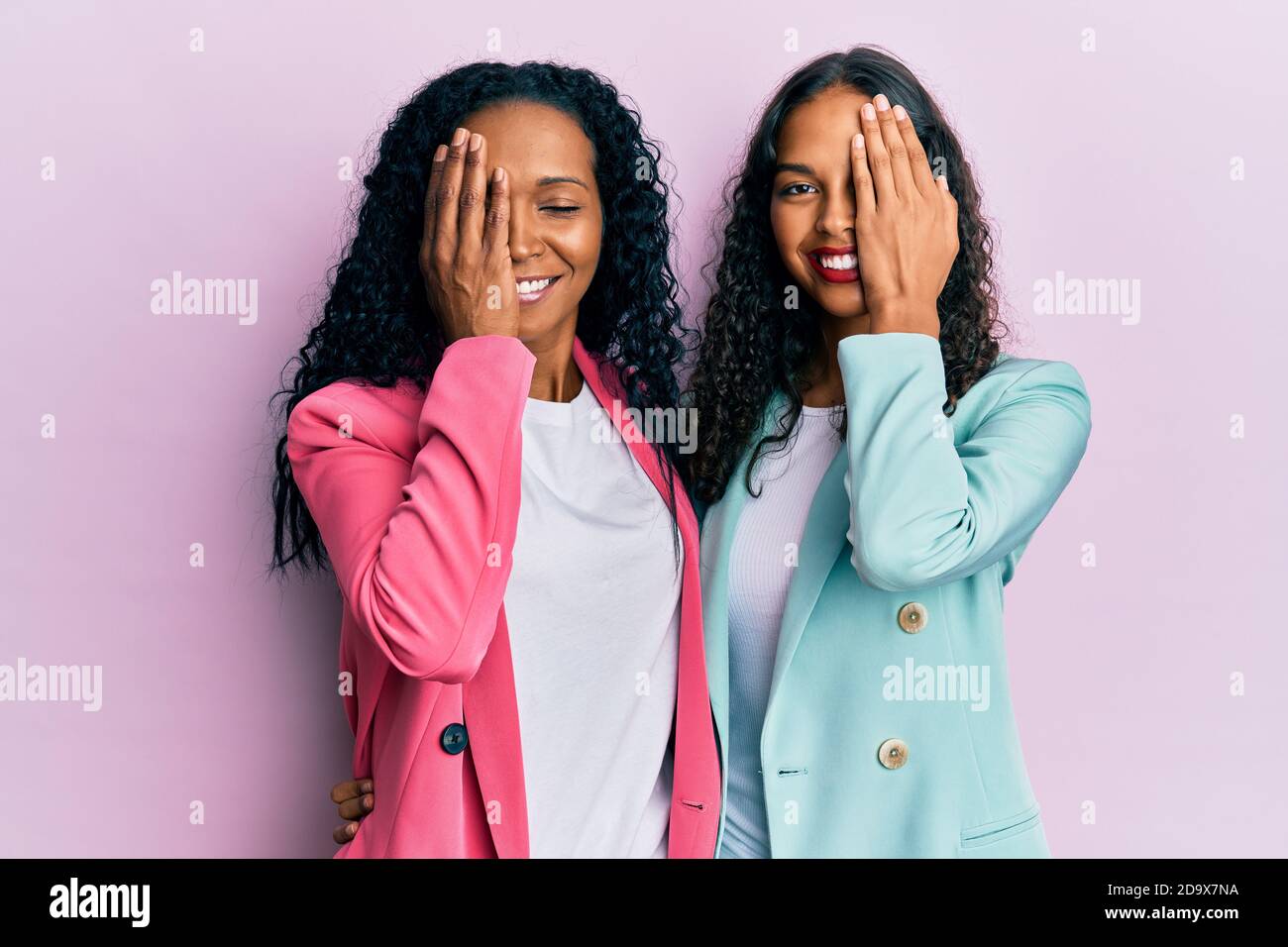 African american mother and daughter wearing business style covering one eye with hand ...