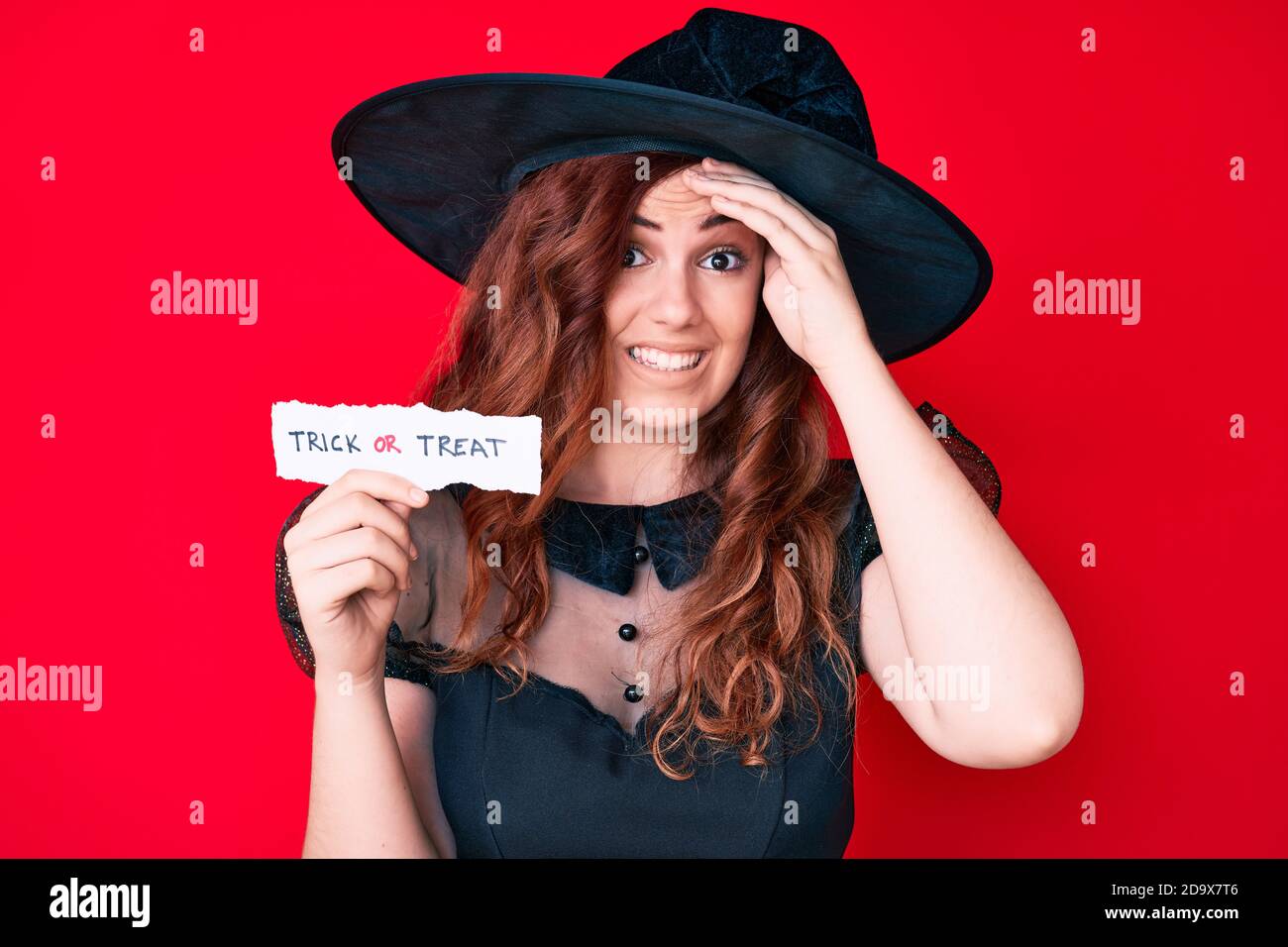 Young beautiful woman wearing witch halloween costume holding paper ...