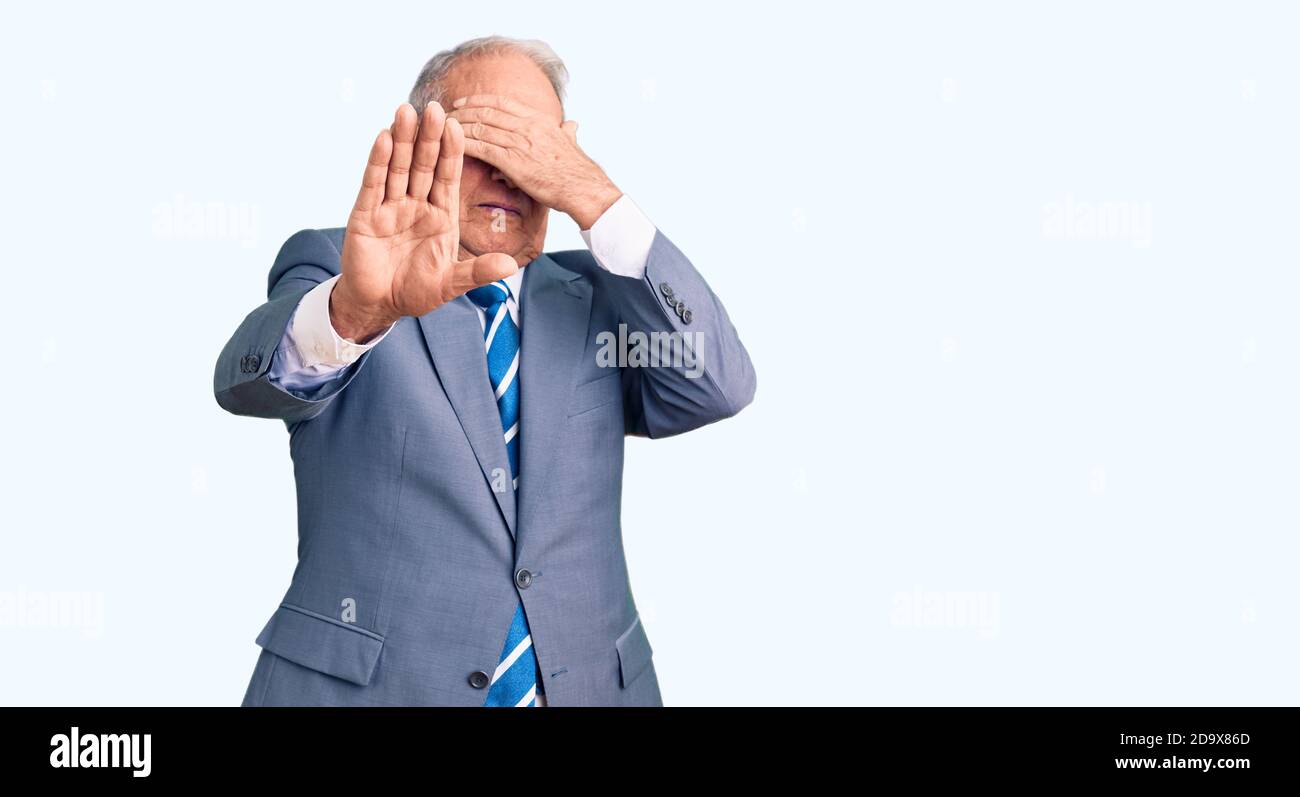 Senior handsome grey-haired man wearing elegant suit covering eyes with ...
