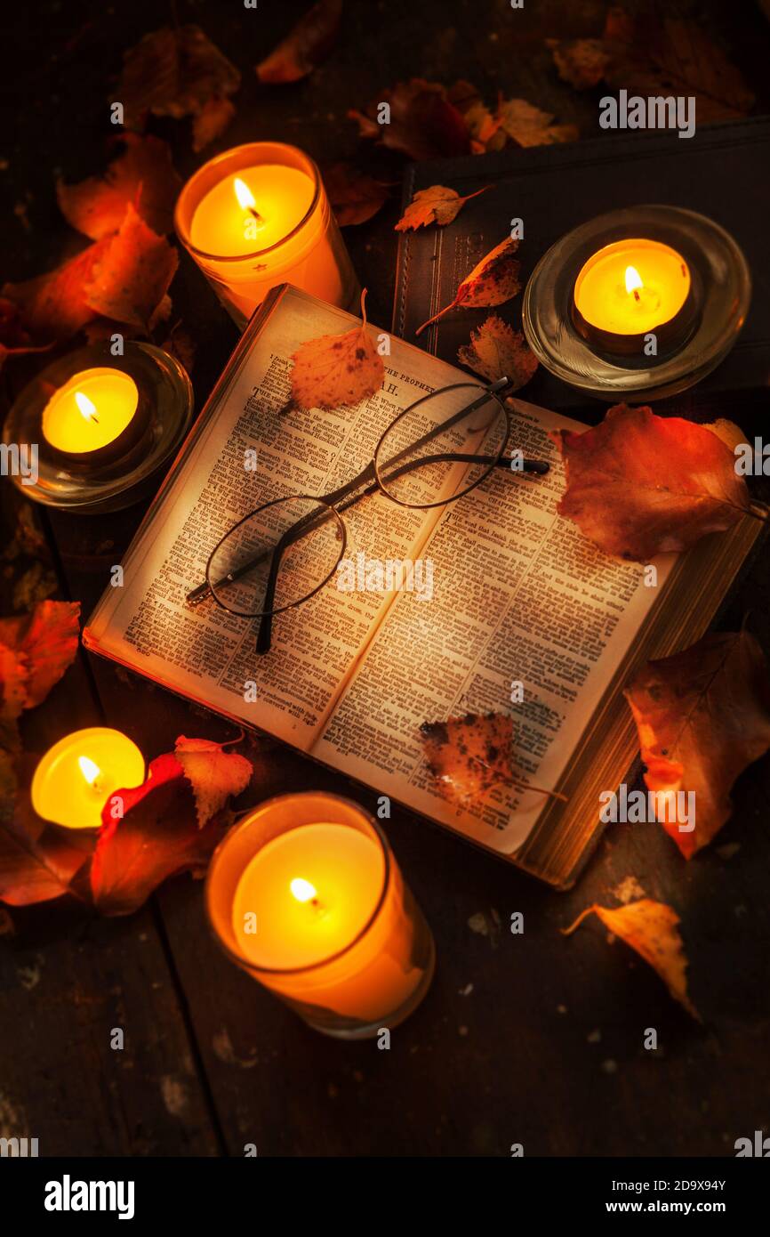 An old book with reading glasses lit by candlelight and decorated with ...