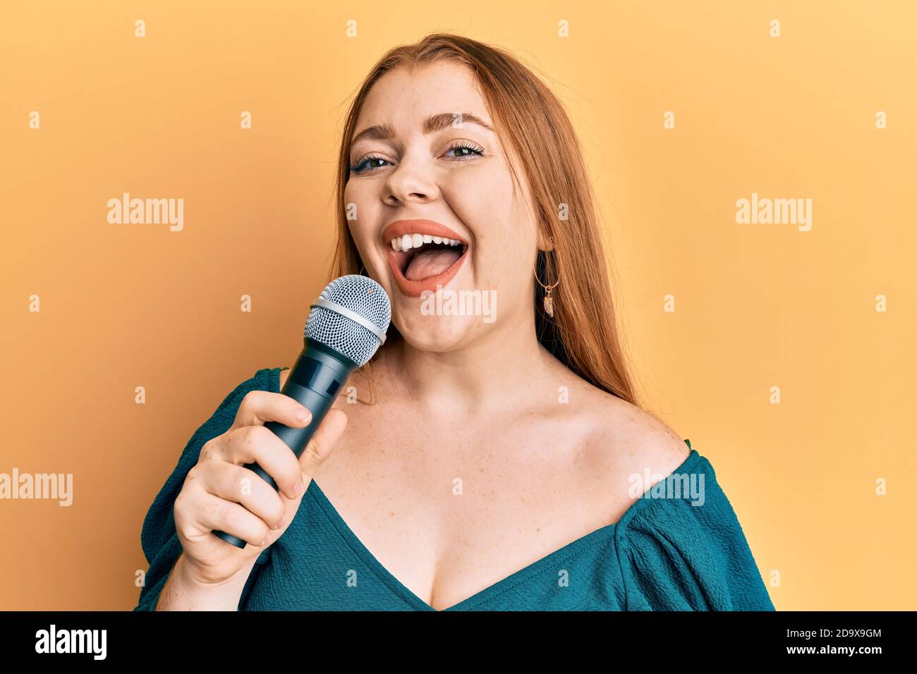 Young beautiful redhead woman singing song using microphone looking ...