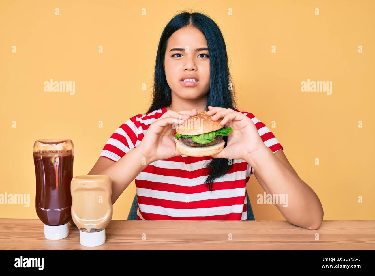 Young asian girl eating a tasty classic burger clueless and confused ...