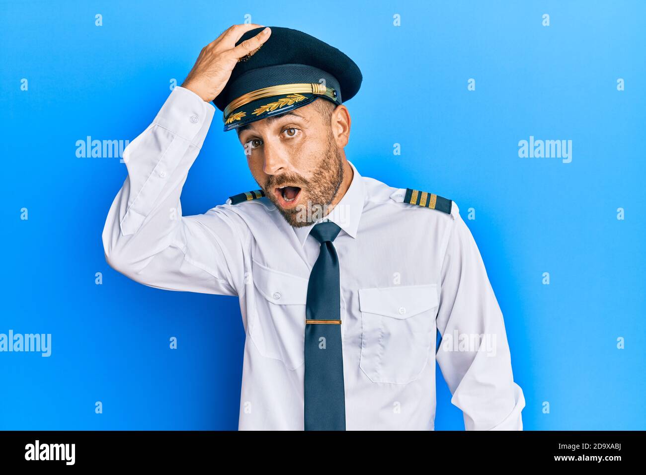Handsome man with beard wearing airplane pilot uniform surprised with ...