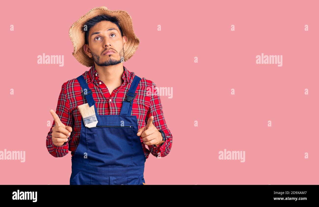 Handsome latin american young man weaing handyman uniform pointing up ...