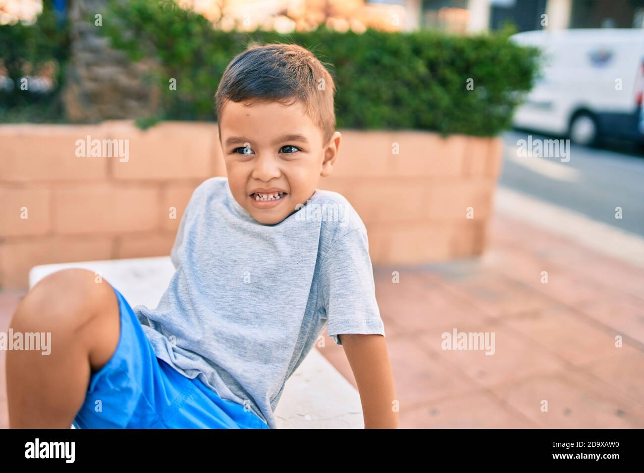 Adorable hispanic boy smiling happy sitting on the bench at the park ...