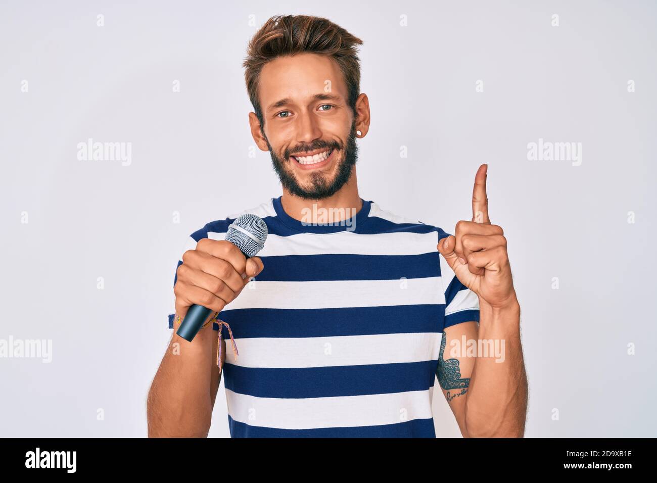 Handsome caucasian man with beard singing song using microphone smiling ...