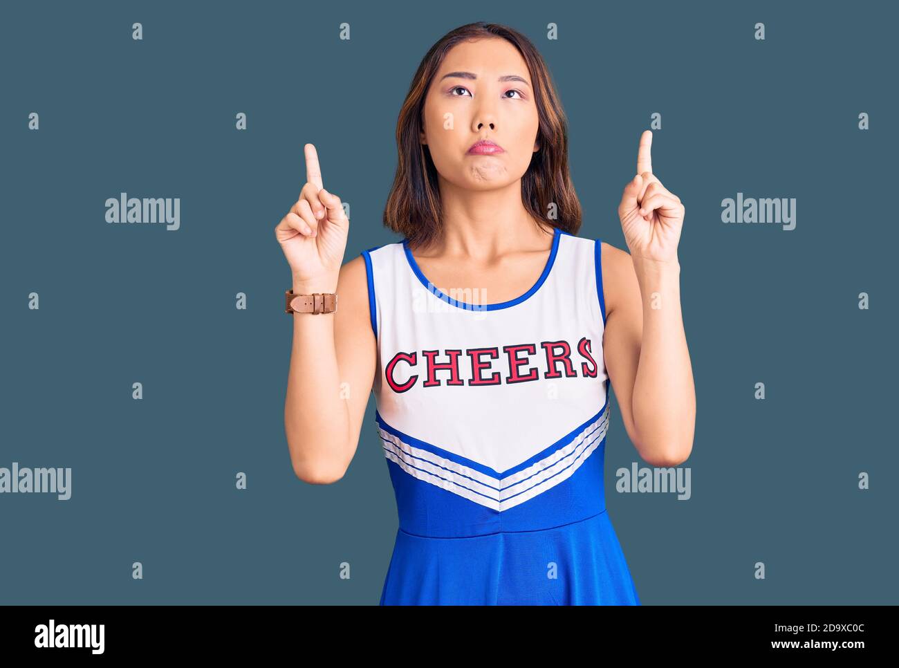 Young beautiful chinese girl wearing cheerleader uniform pointing up ...