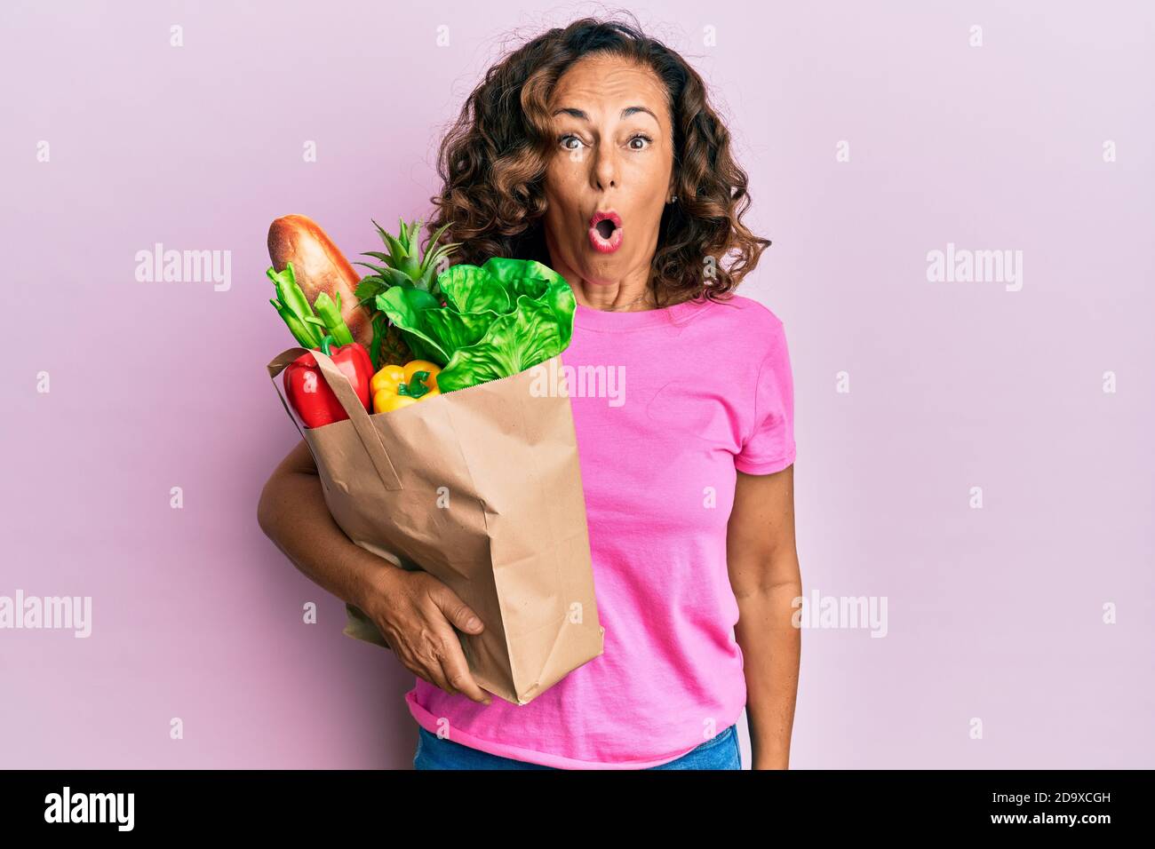 Middle age hispanic woman holding paper bag with bread and groceries ...