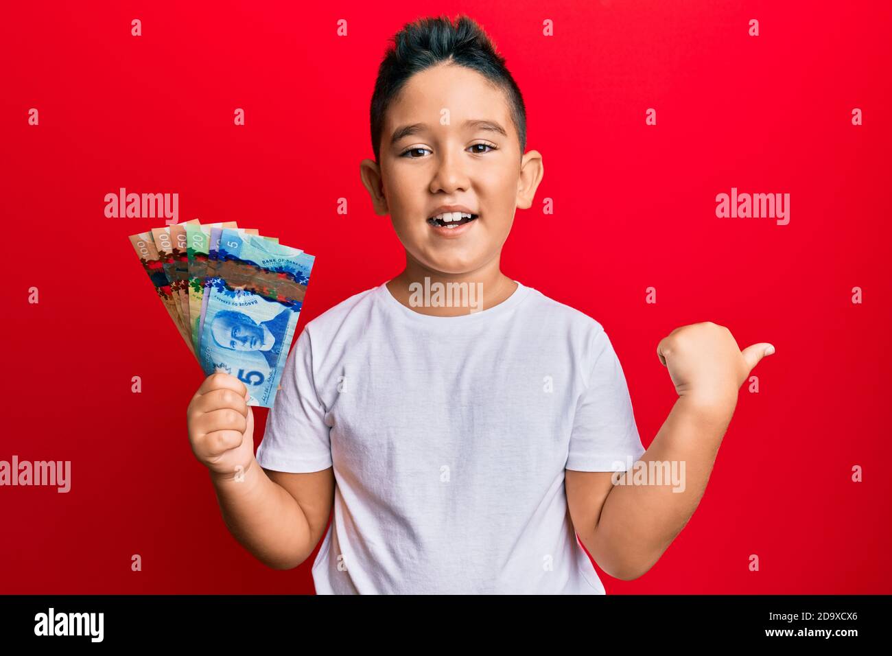 Little boy hispanic kid holding canadian dollars pointing thumb up to ...