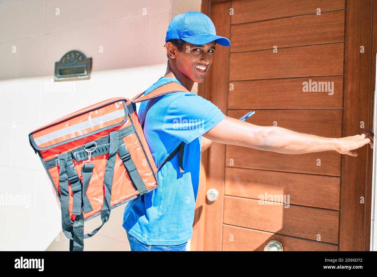 African delivery man wearing courier uniform outdoors using smartphone ...