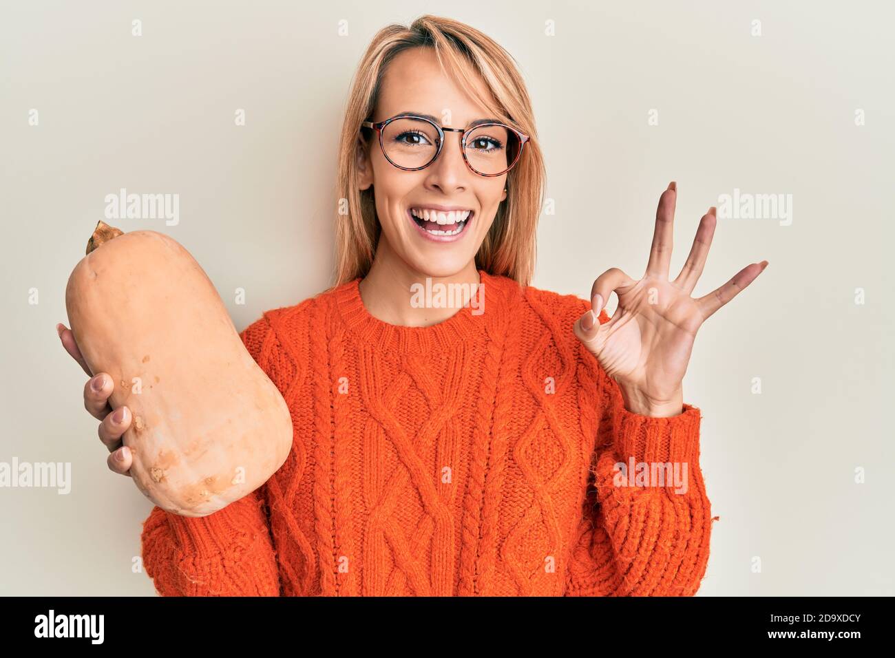 Beautiful blonde woman holding healthy fresh pumpkin doing ok sign with ...