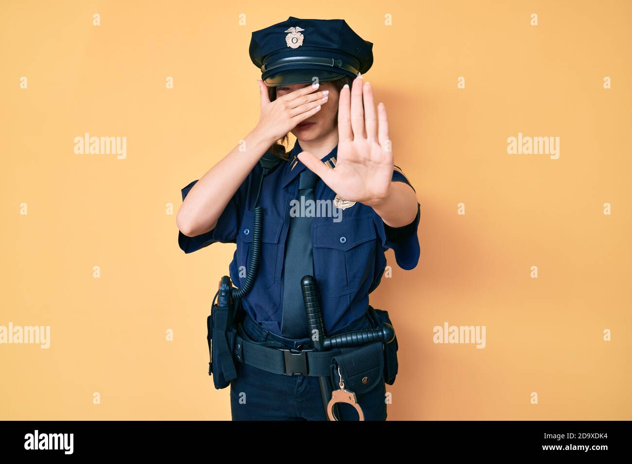 Young beautiful woman wearing police uniform covering eyes with hands ...