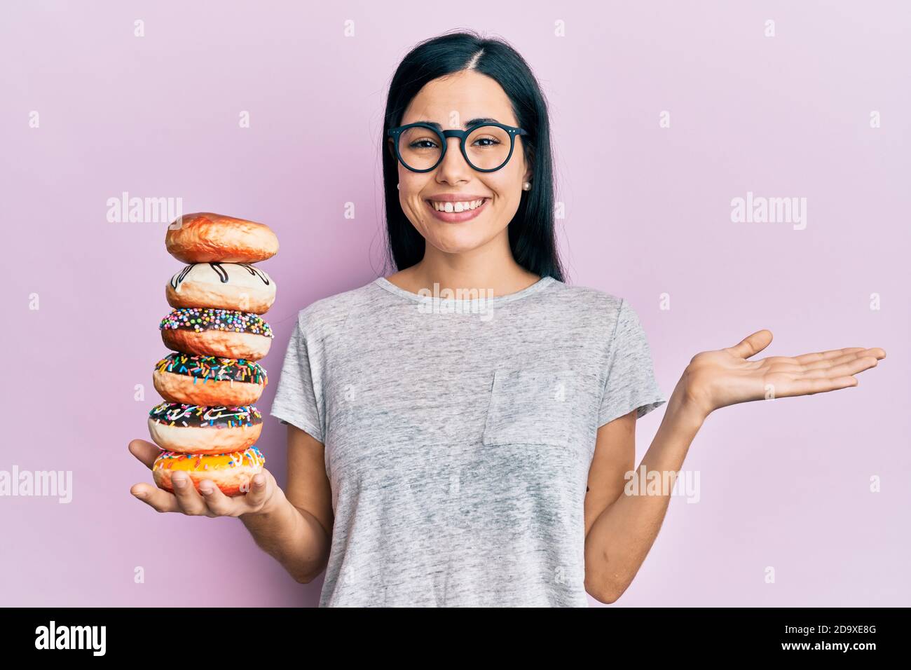 Beautiful young woman holding pile of tasty colorful doughnuts ...