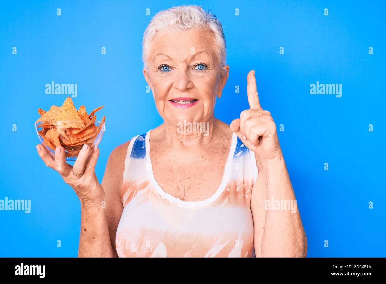 Senior beautiful woman with blue eyes and grey hair holding nachos ...