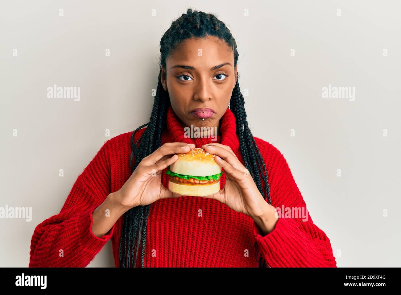 African american woman with braids eating hamburger depressed and worry ...