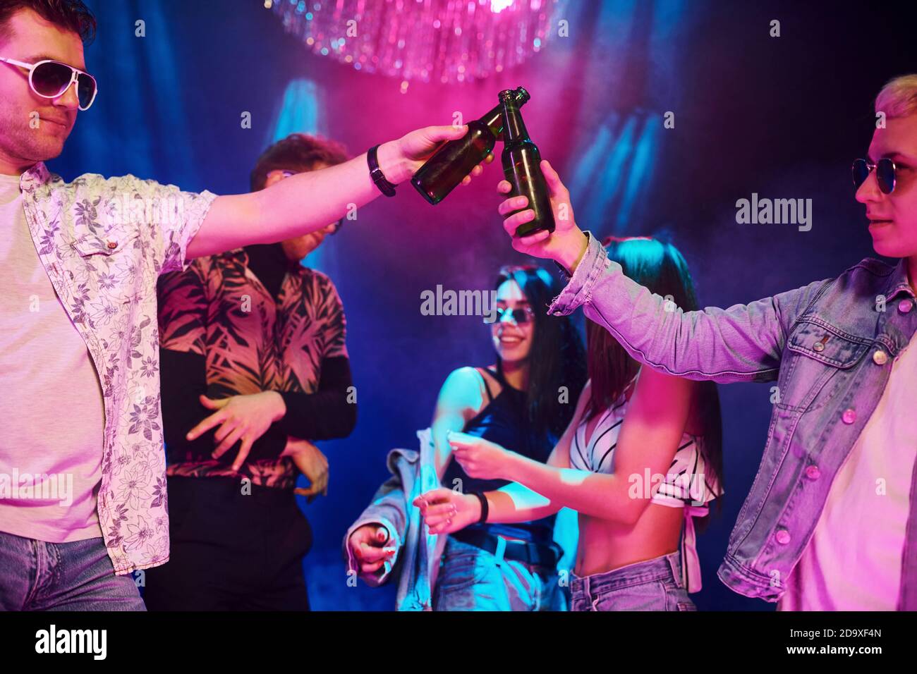 Celebrating and knocking bottles with alcohol. Young people is having ...