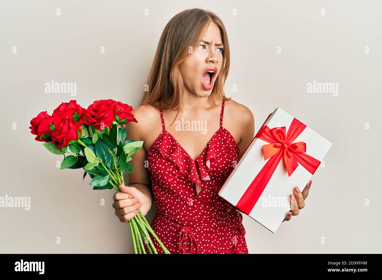 Beautiful young blonde woman holding anniversary present and bouquet of ...