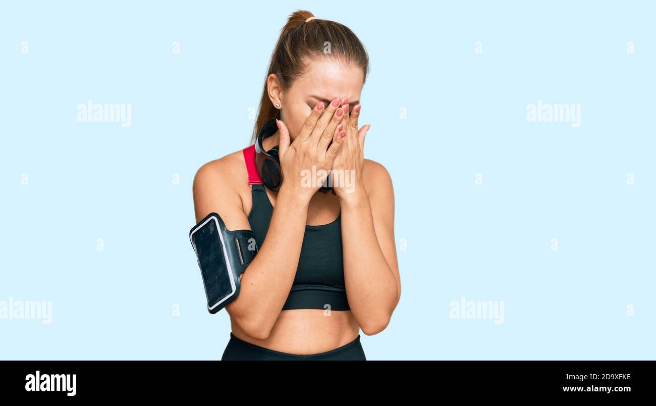 Beautiful blonde woman wearing gym clothes and using headphones with ...