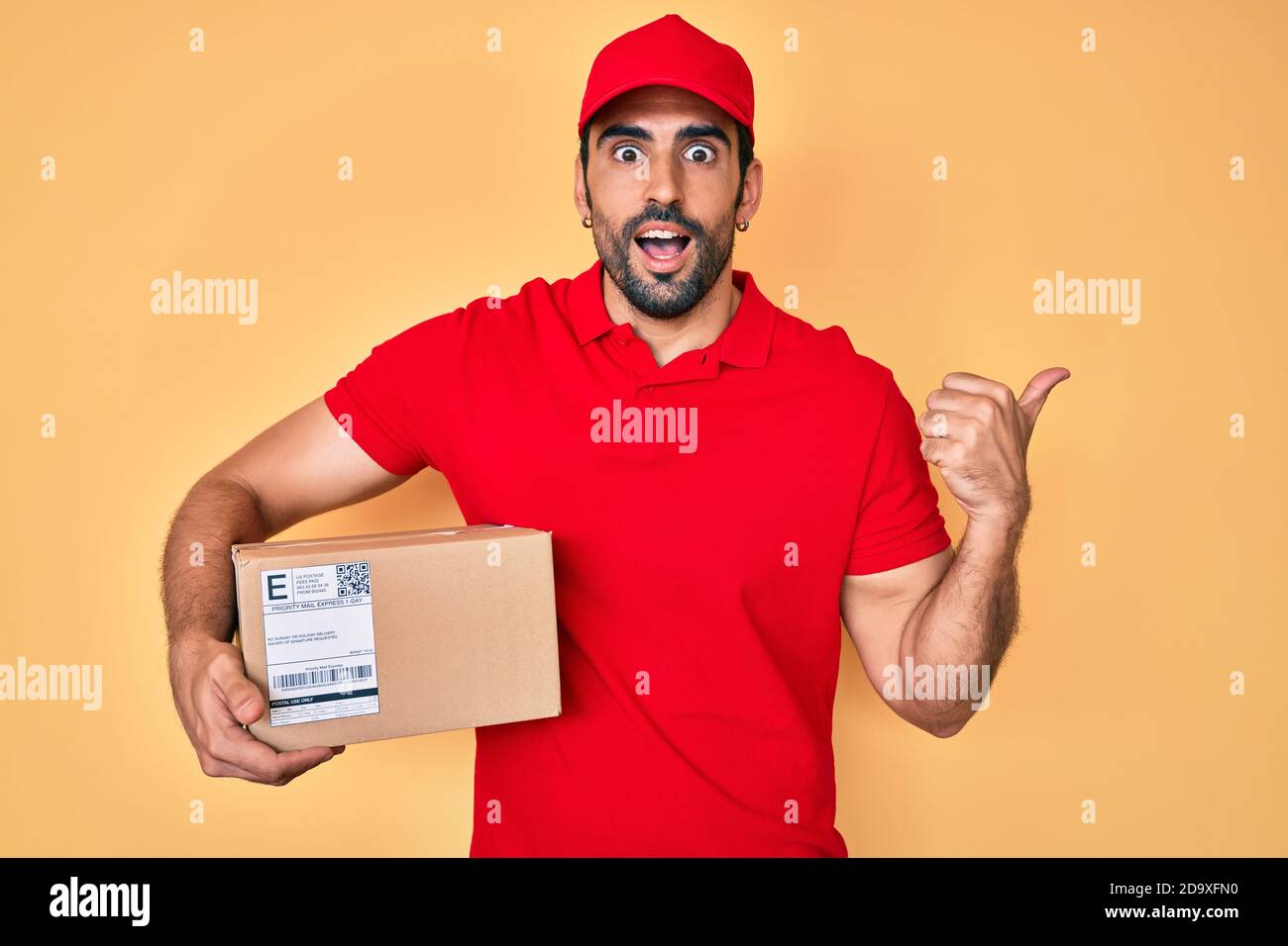 Handsome hispanic man with beard holding delivery package pointing ...