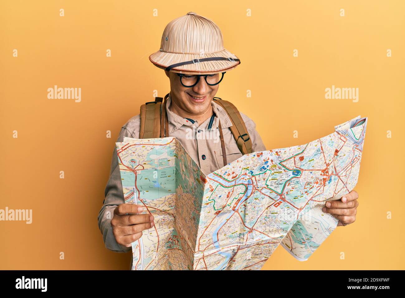 Middle age bald man wearing explorer hat holding map smiling with a ...