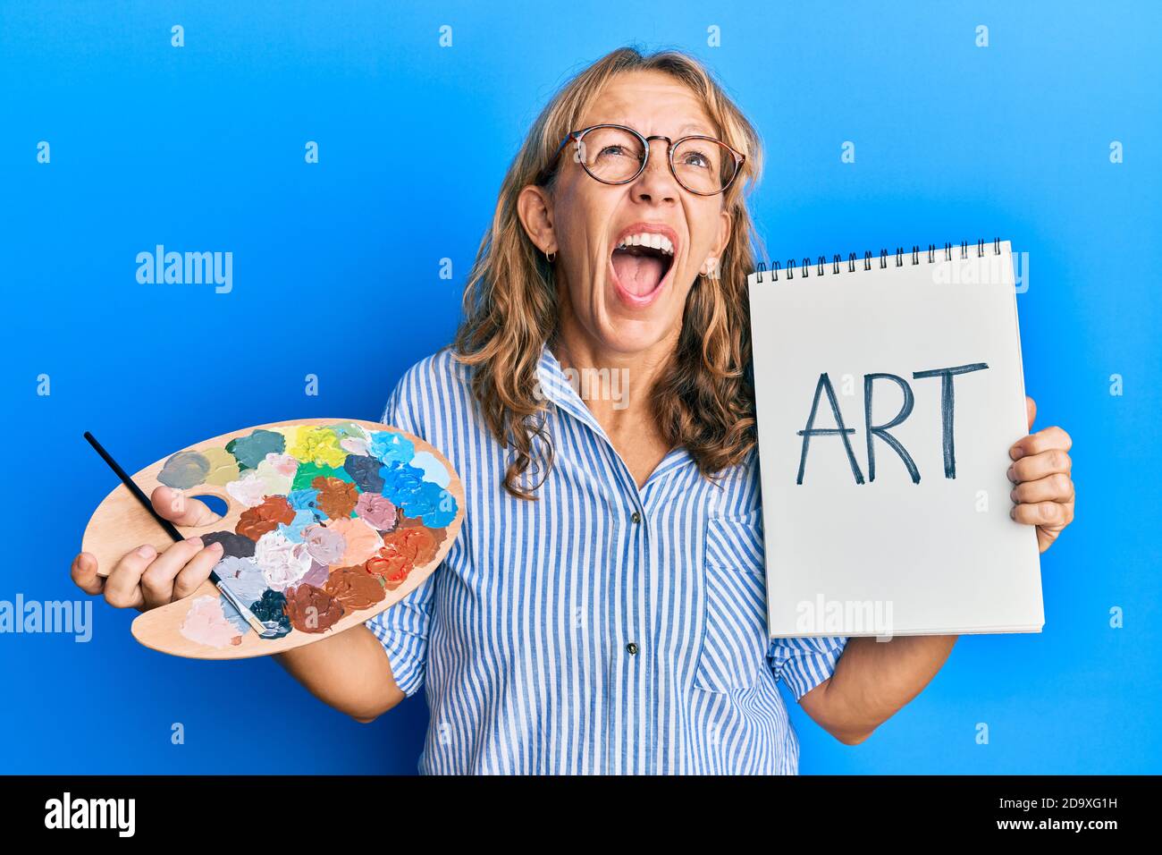 Middle age blonde woman holding painter palette and notebook angry and ...