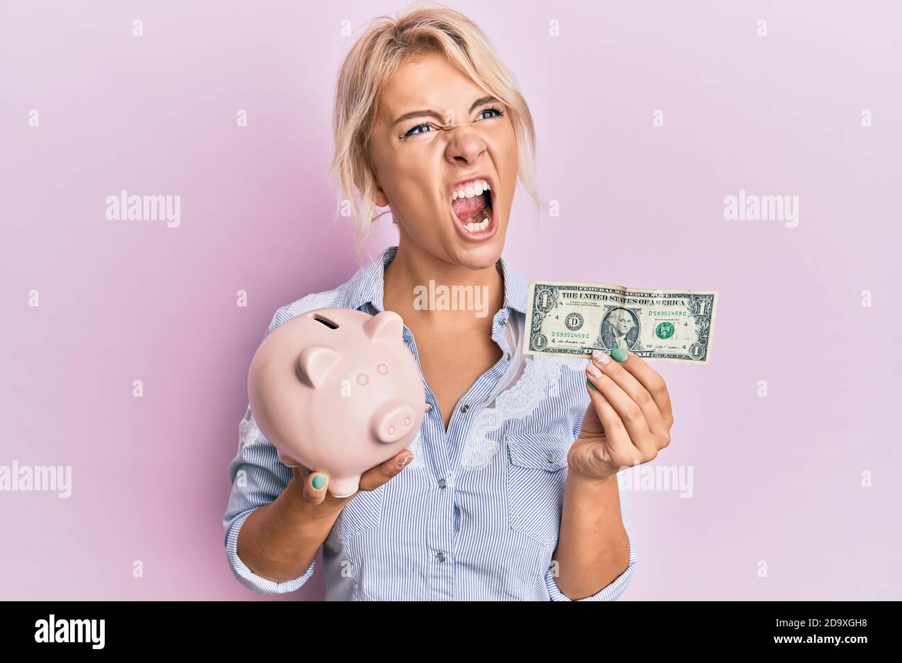 Young blonde girl holding dollar and piggy bank angry and mad screaming ...