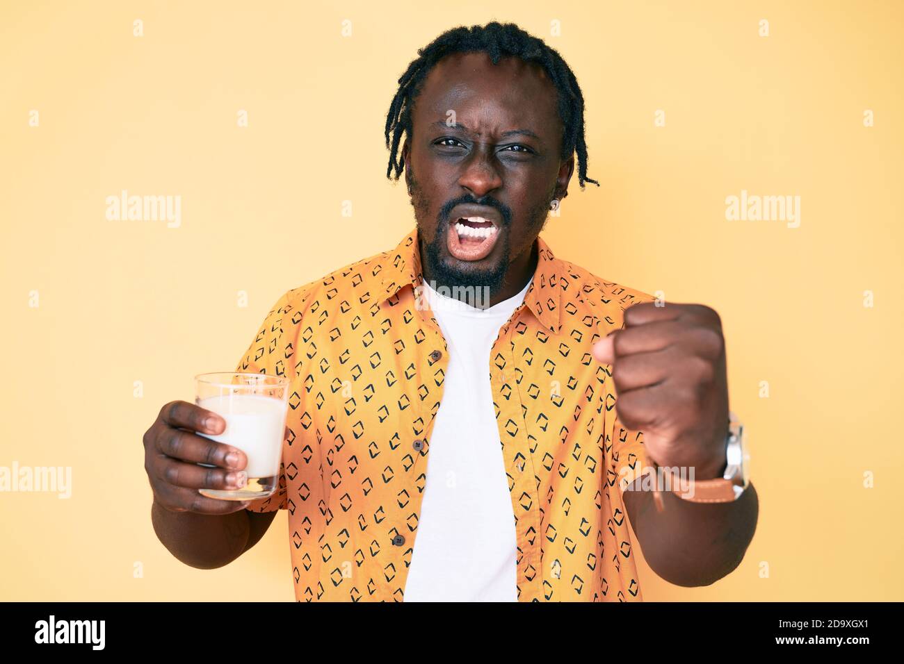 Young african american man with braids holding glass of milk annoyed ...