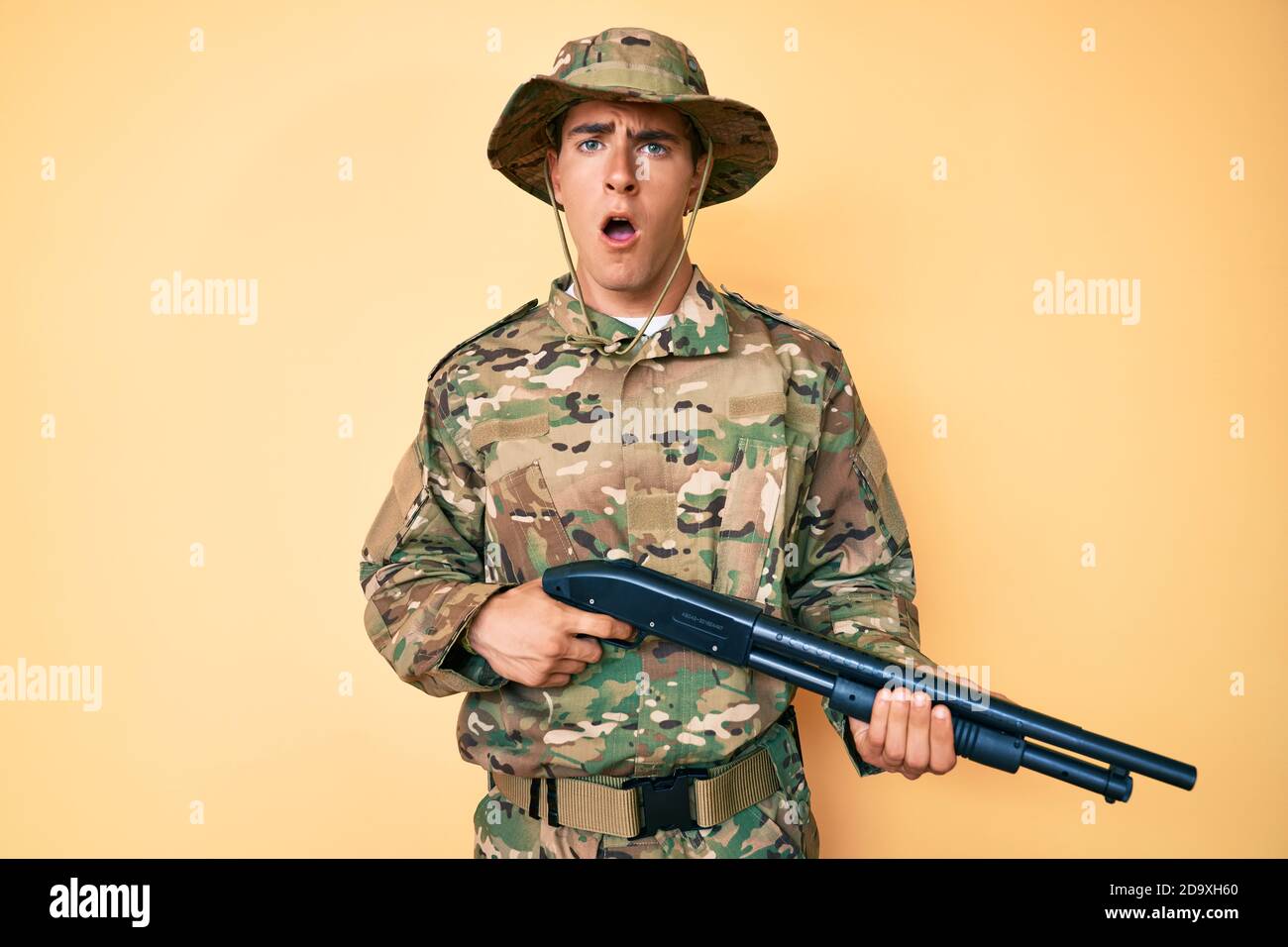 Young handsome man wearing camouflage army uniform holding shotgun in ...