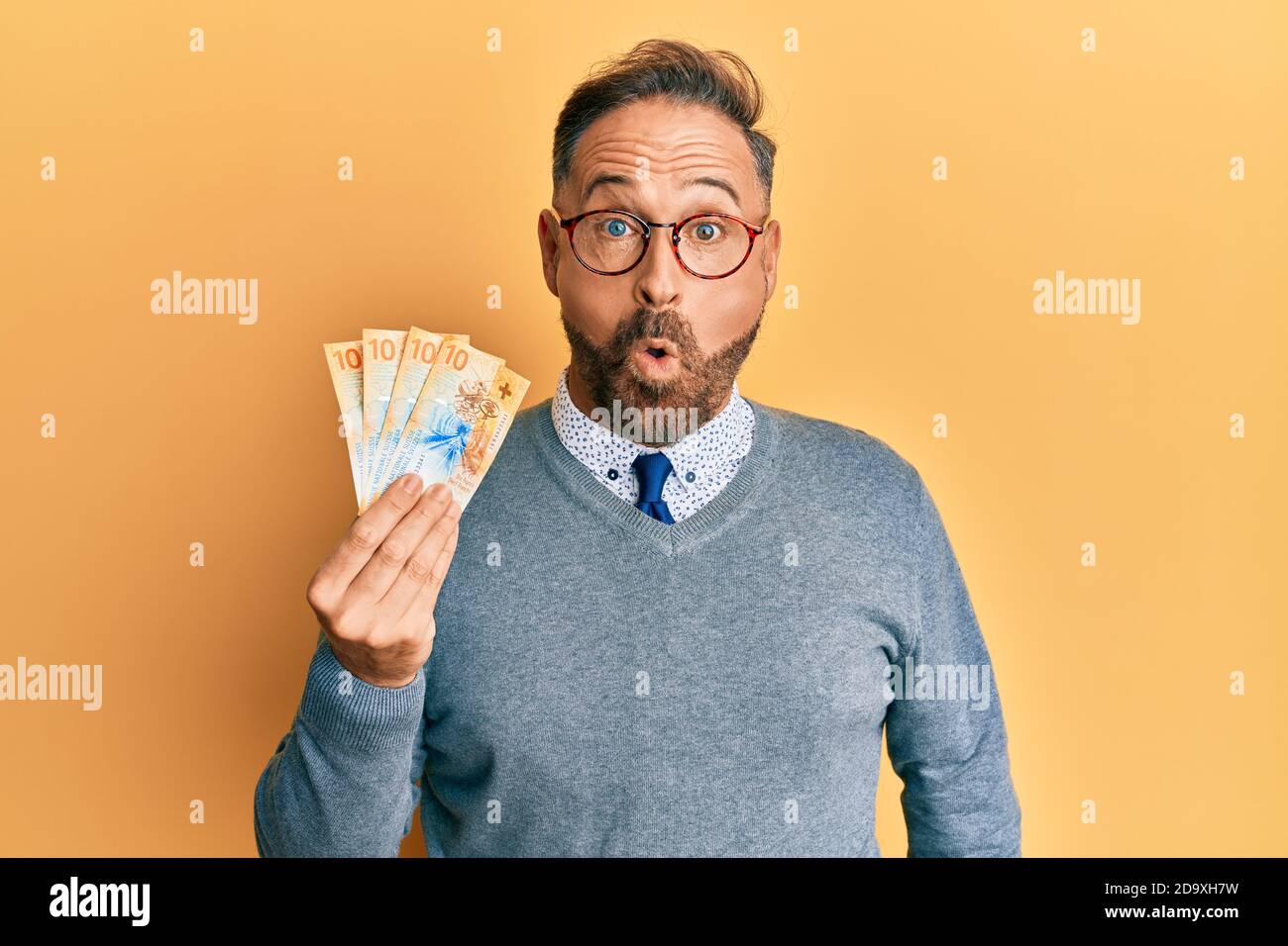 Handsome middle age man holding swiss franc banknotes scared and amazed ...