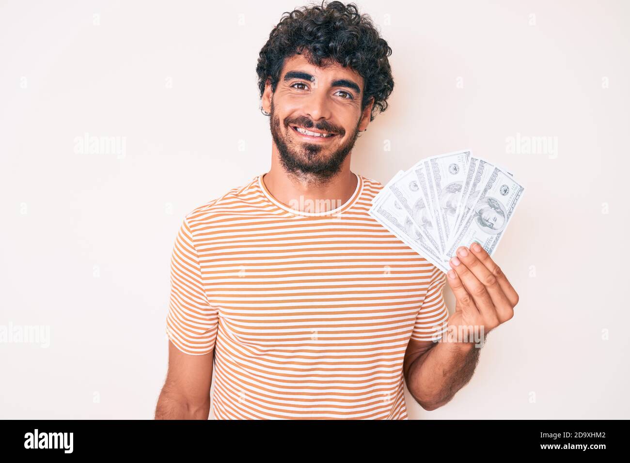 Handsome young man with curly hair and bear holding money bag with ...