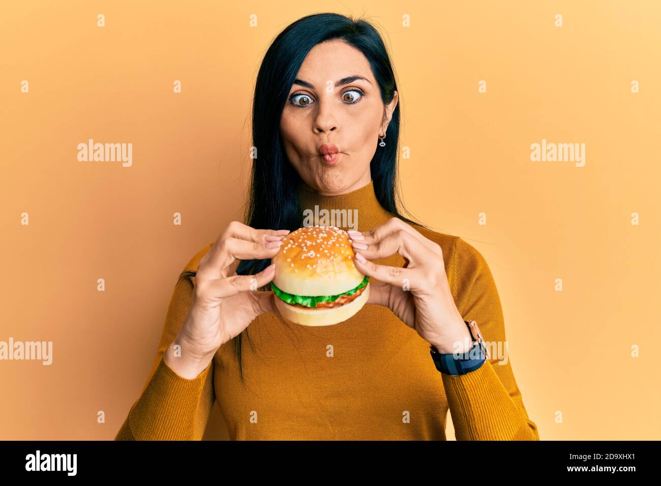 Young caucasian woman eating a tasty classic burger making fish face ...