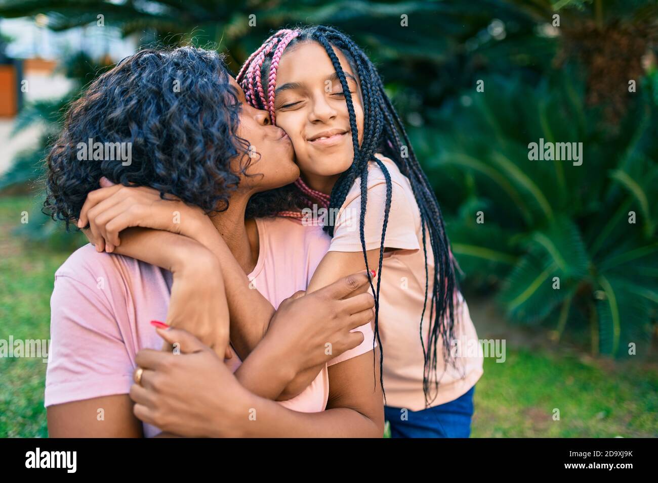 Beautiful african american mother and daughter kissing and hugging. Standing with smile on face ...