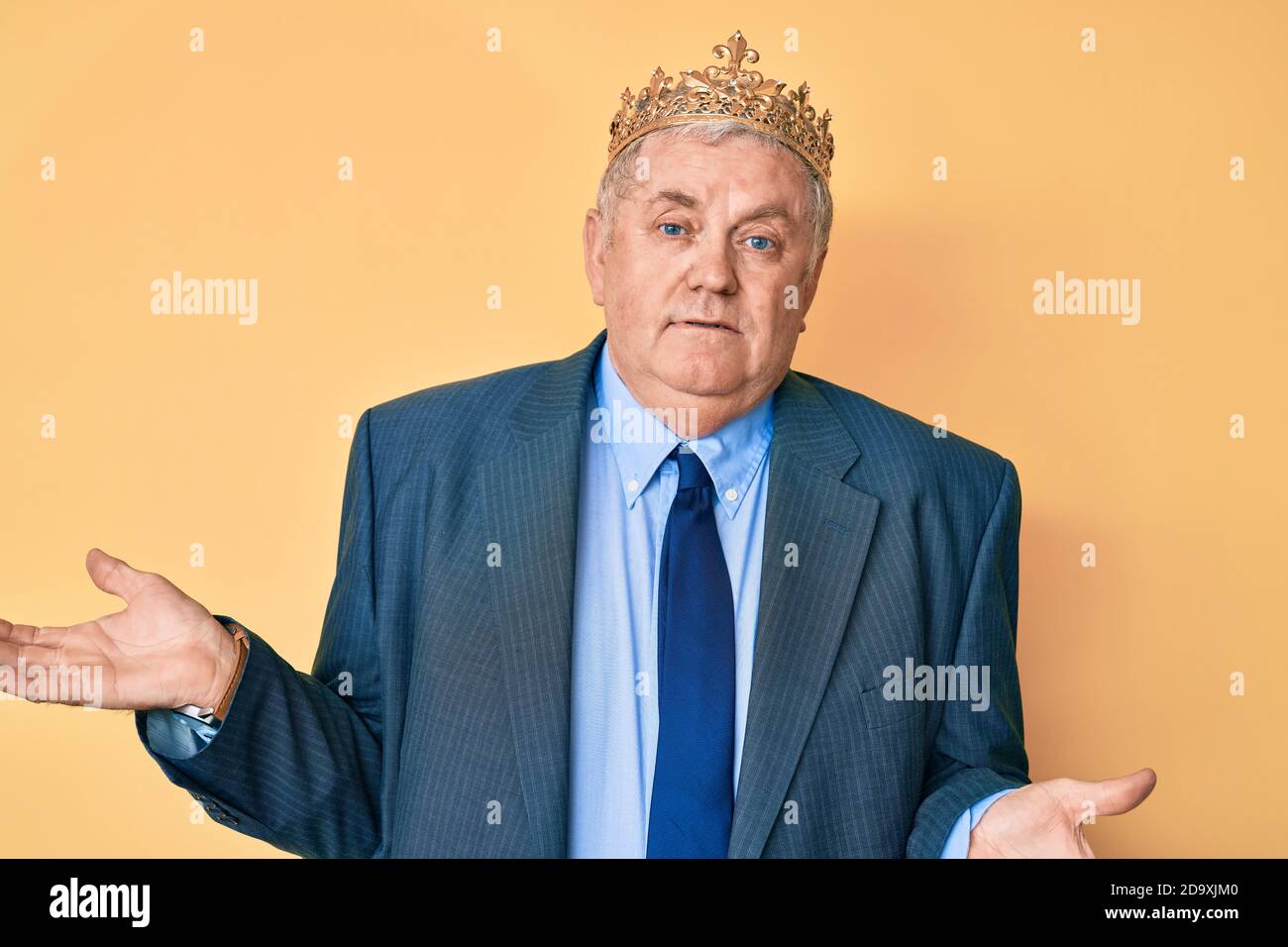 Senior grey-haired man wearing business suit and king crown clueless ...