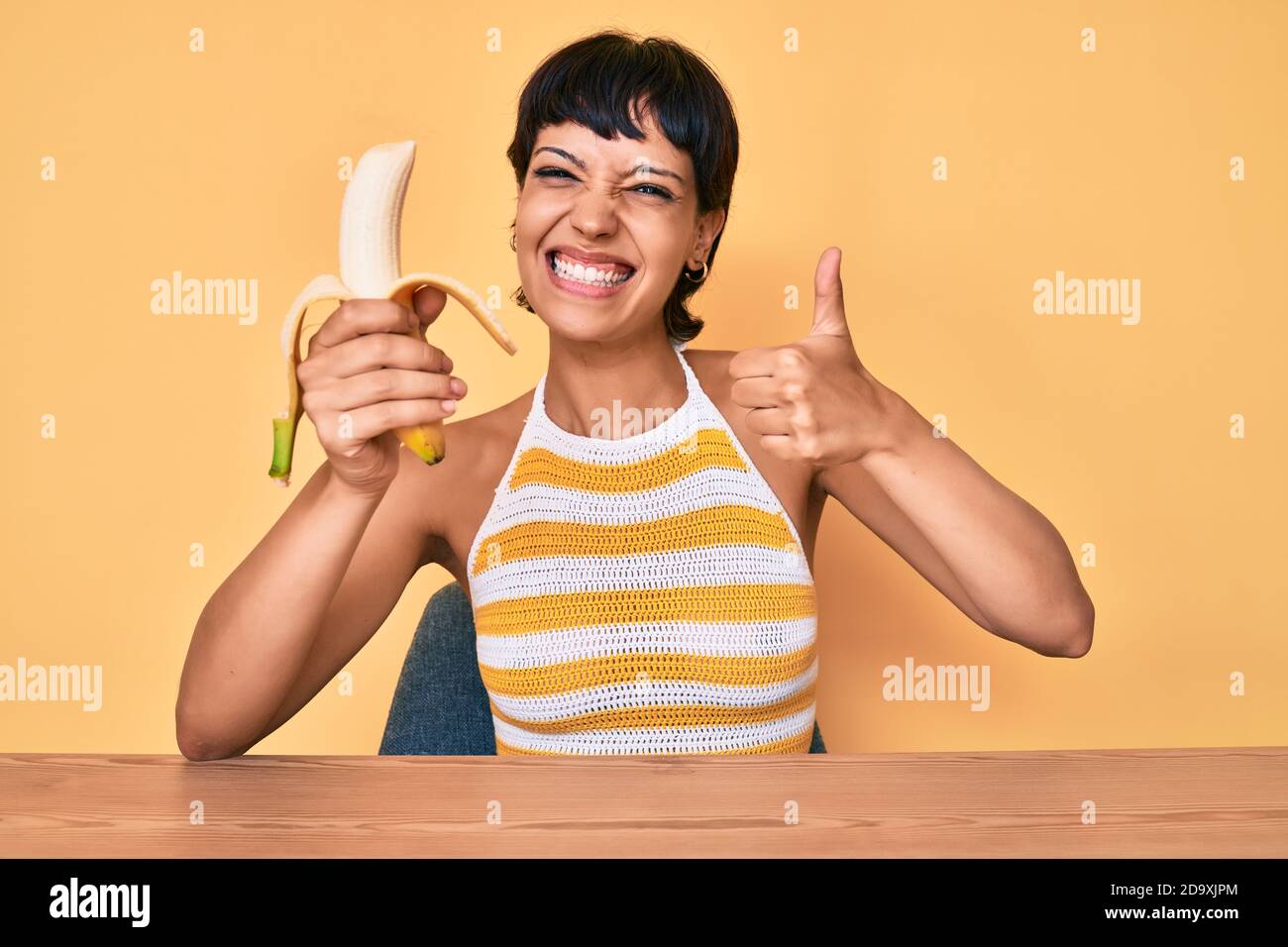 Brunette teenager girl eating banana as healthy snack smiling happy and ...