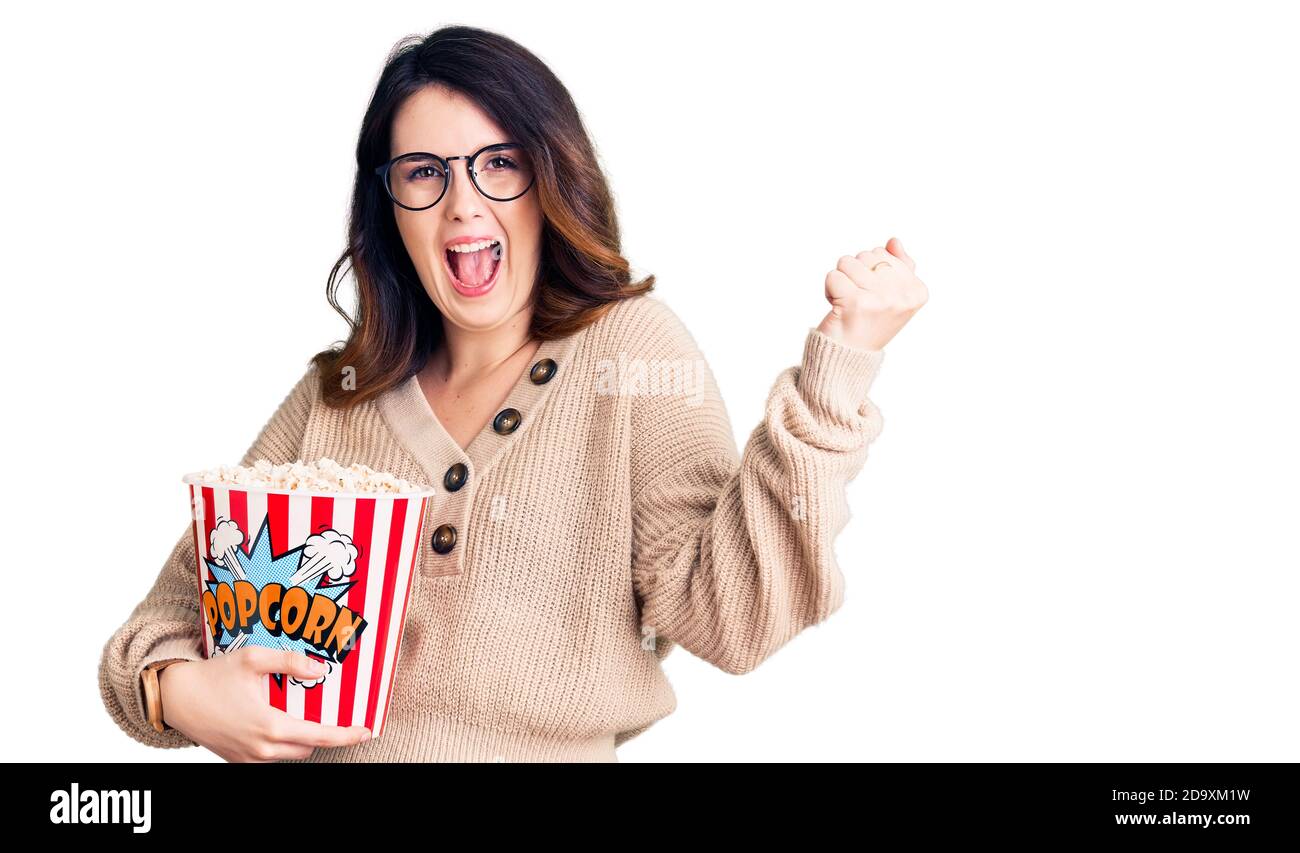 Beautiful young brunette woman eating popcorn screaming proud ...