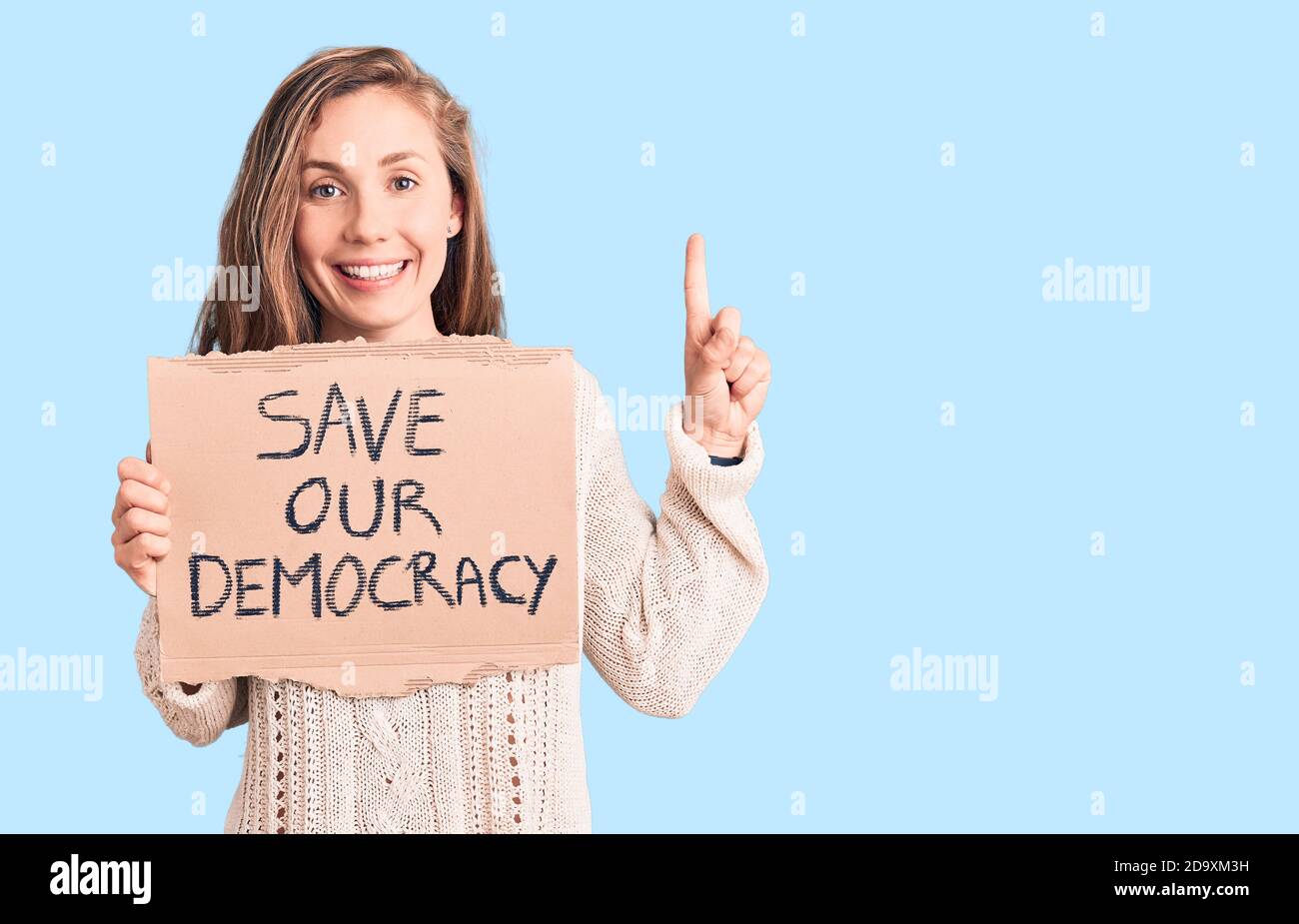 Young beautiful blonde woman holding save our democracy banner ...