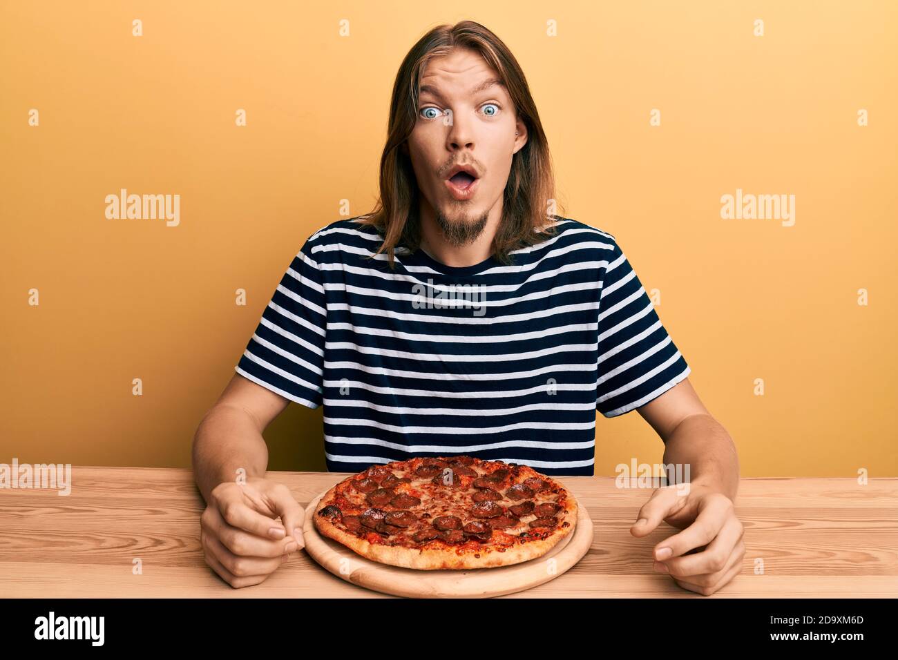 Handsome caucasian man with long hair eating tasty pepperoni pizza ...