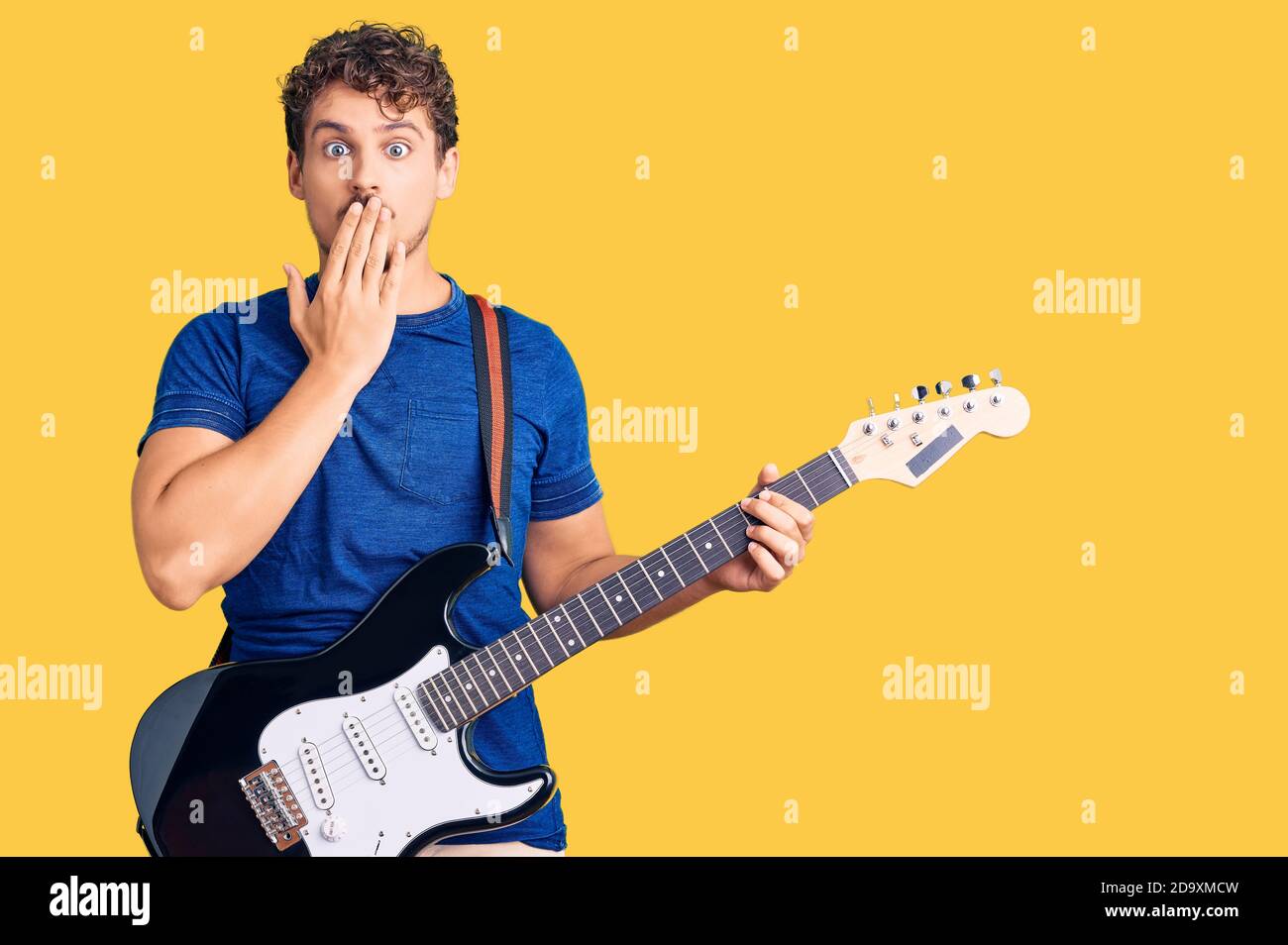Young handsome man with curly hair playing electric guitar covering ...