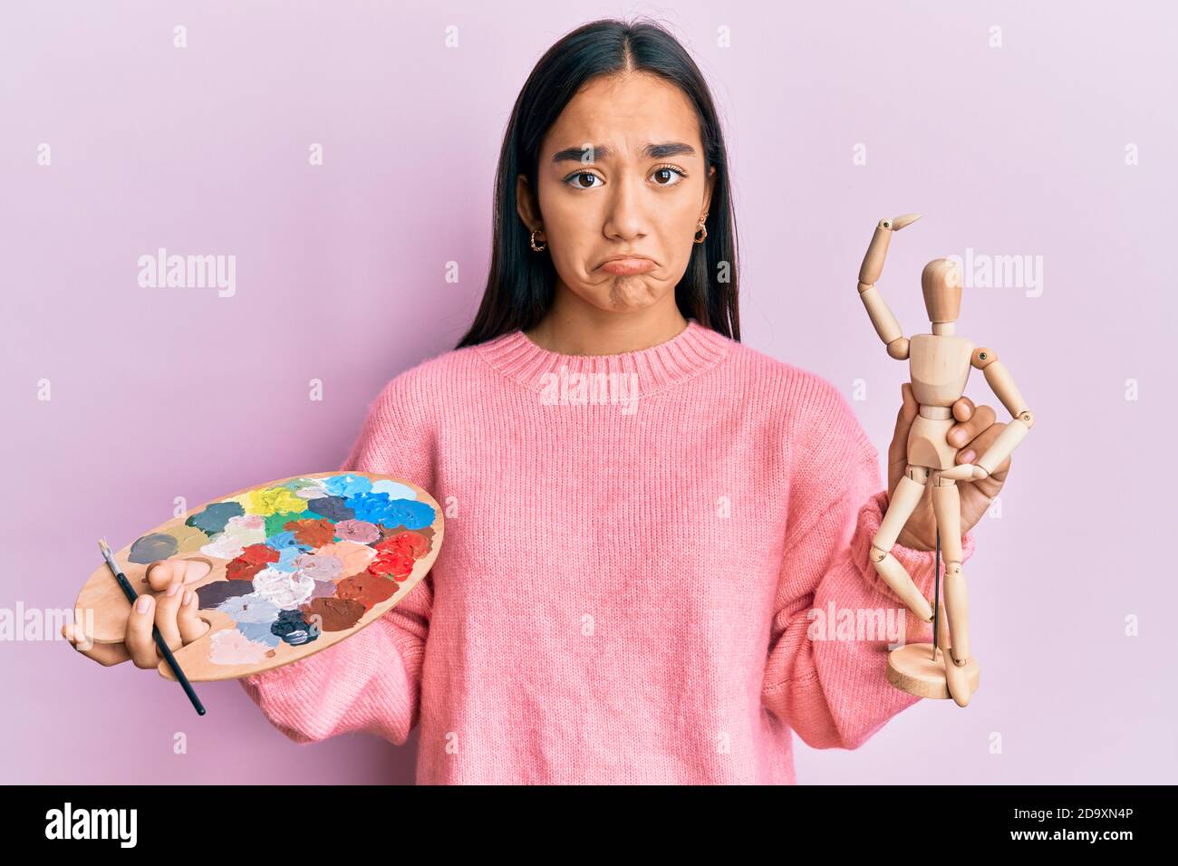Young asian woman holding painter palette and art manikin depressed and ...