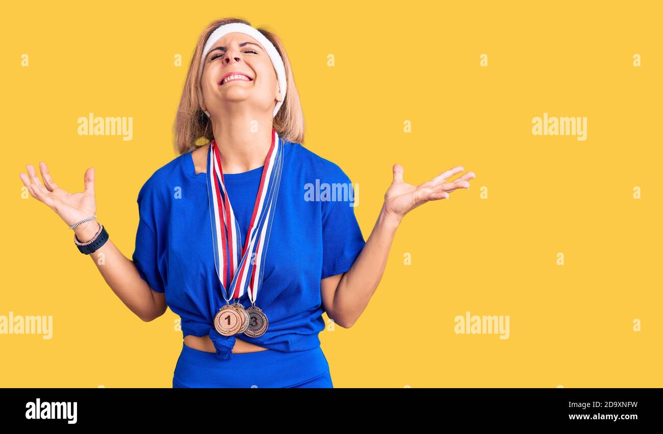 Young blonde woman wearing winner medals celebrating mad and crazy for ...