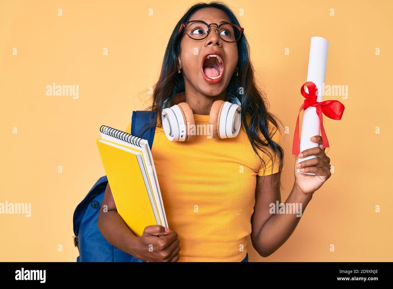 Young indian girl wearing student backpack holding diploma angry and ...