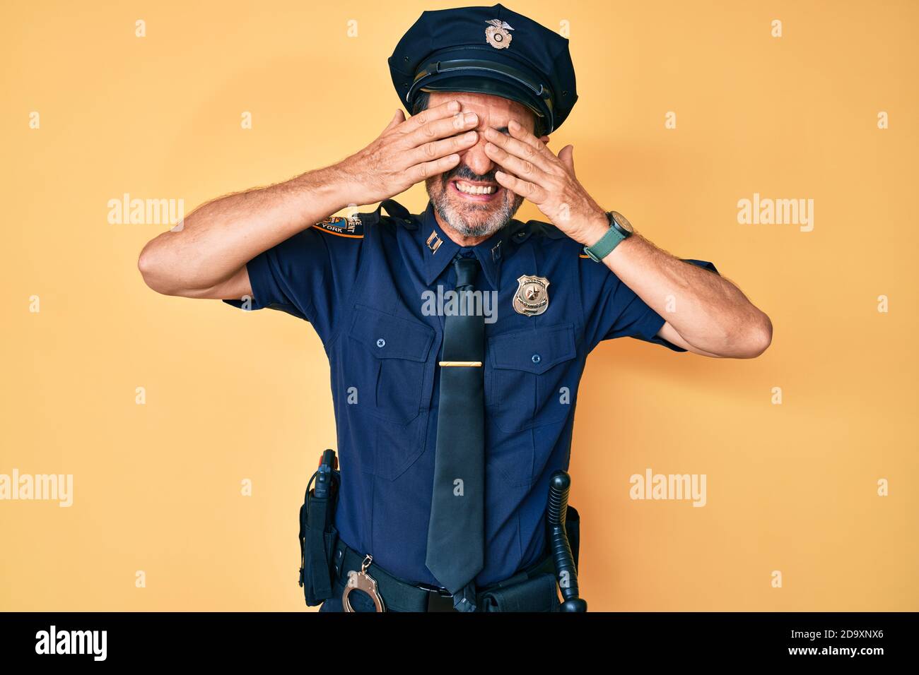 Middle age hispanic man wearing police uniform covering eyes with hands ...