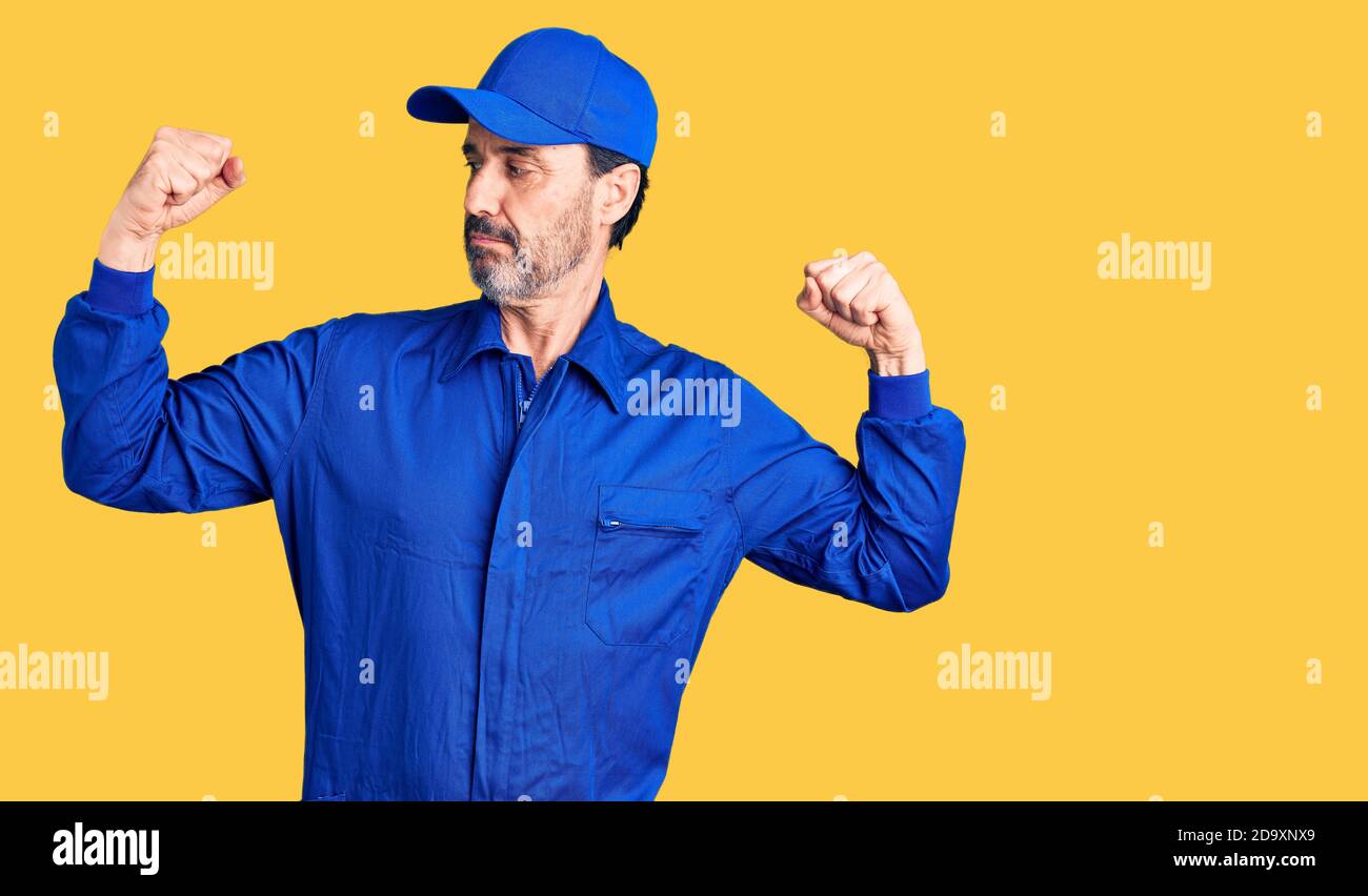 Middle age handsome man wearing mechanic uniform showing arms muscles ...