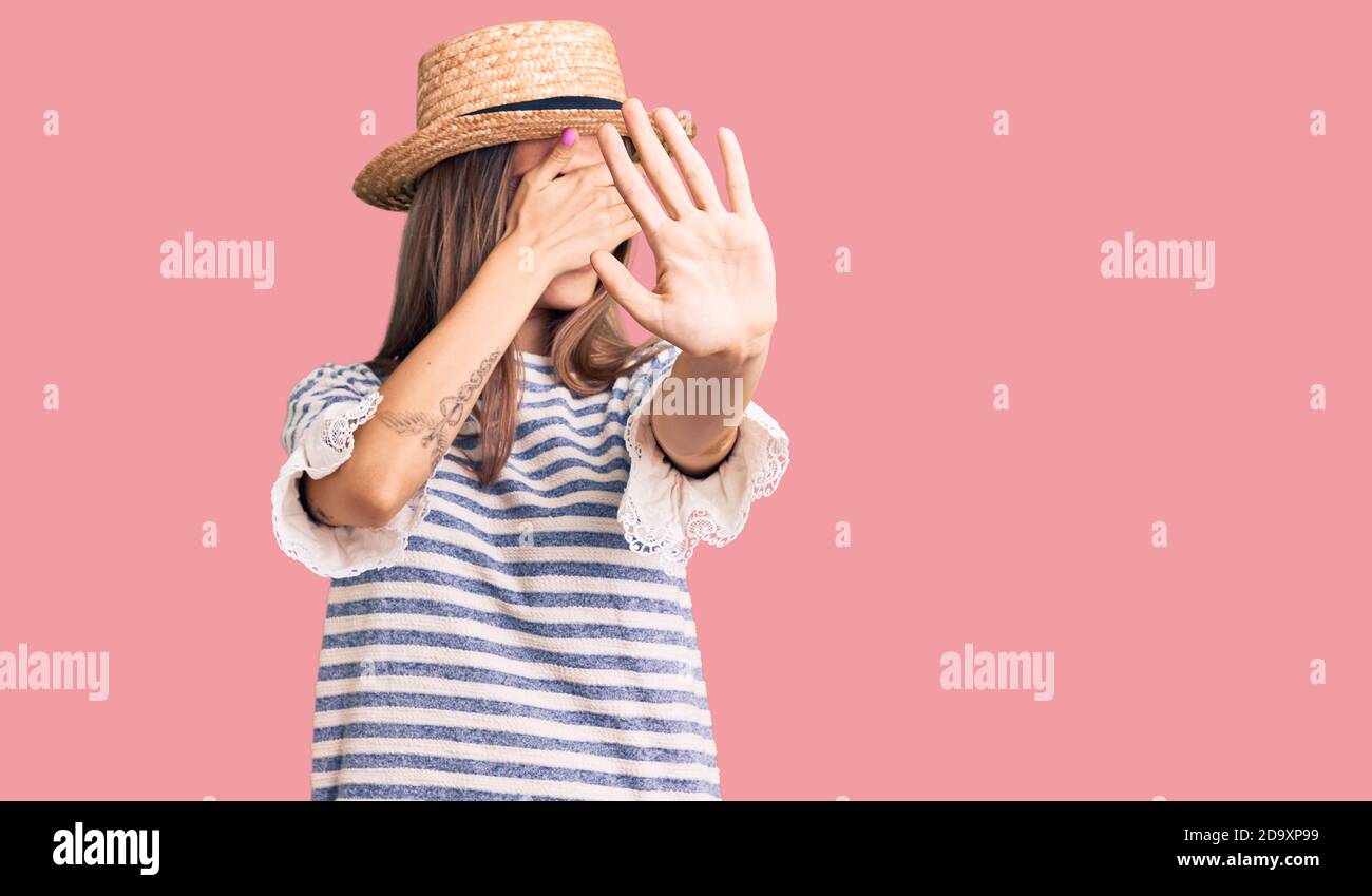 Beautiful caucasian woman wearing summer hat covering eyes with hands ...